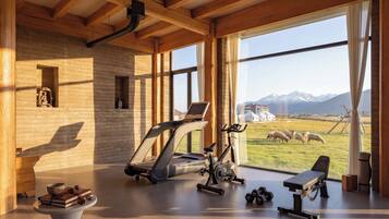 Um quarto espaçoso com uma janela grande, esteira ergométrica, bicicleta de exercício e um banco.