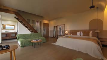 Quarto de hotel com cama, sofá verde, pequena mesa com um livro, espelho e escada.