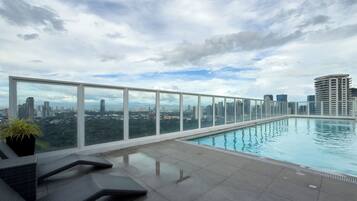 Piscina no terraço com vista para o horizonte urbano, cercada por grades de vidro e espreguiçadeiras.