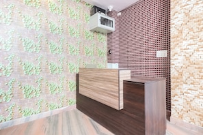 Uma área de recepção com balcão de madeira, parede de tijolos com folhagem verde e parede decorada com um padrão geométrico em grade.