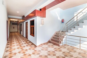 Um corredor com piso estampado, escada com corrimão de metal e extintor de incêndio fixado na parede.