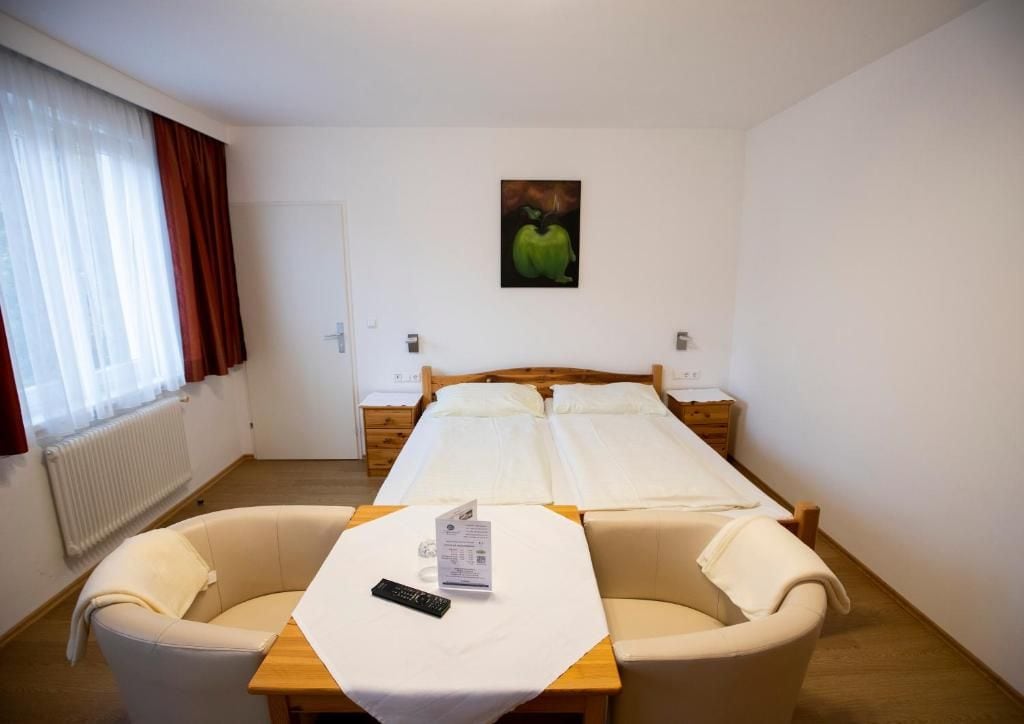 Quarto de hotel com cama, duas mesas de cabeceira, uma mesinha com um controle remoto e uma cadeira.