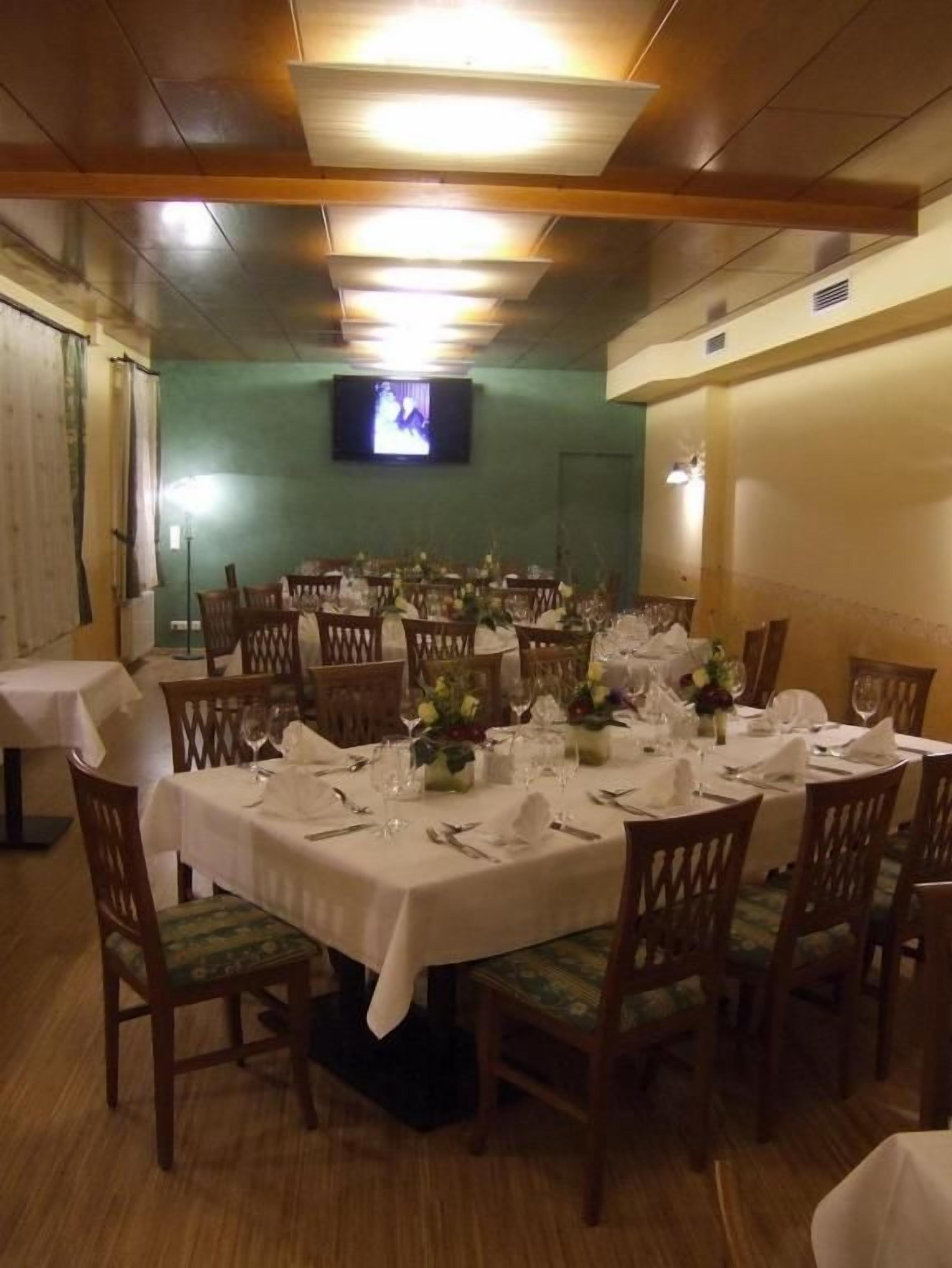 Uma sala de jantar com várias mesas postas para refeição, cadeiras e uma tela de televisão na parede.
