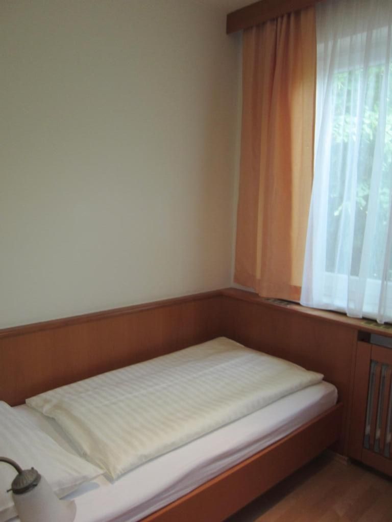 Uma cama de solteiro com cabeceira de madeira num quarto com janela.