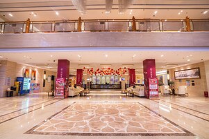 Um hall de hotel com piso de mármore, balcão de recepção, área de estar, máquinas de venda automática e uma varanda.