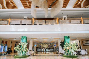 Um saguão de hotel com balcão de recepção, área de estar e uma decoração com plantas.