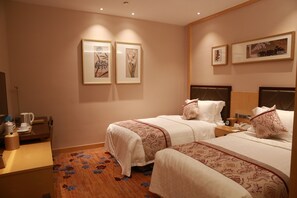 Quarto de hotel com duas camas, uma escrivaninha com cafeteira e quadros nas paredes.