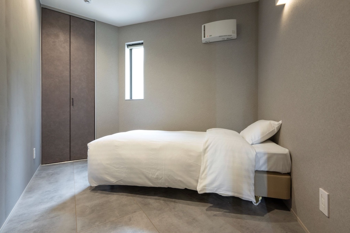 Quarto com cama, guarda-roupa, janela e aparelho de ar condicionado.