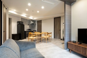 Uma sala de estar moderna com sofá, mesa de jantar, cadeiras, TV e área de cozinha com eletrodomésticos.