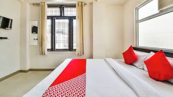 Quarto de hotel com cama, televisão, janela com cortinas e vista para o exterior.