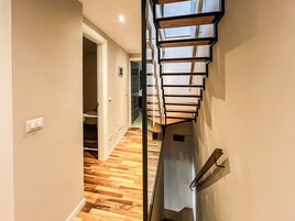 Um interior moderno com piso de madeira, escada com corrimão de vidro e porta que dá para outro cômodo.