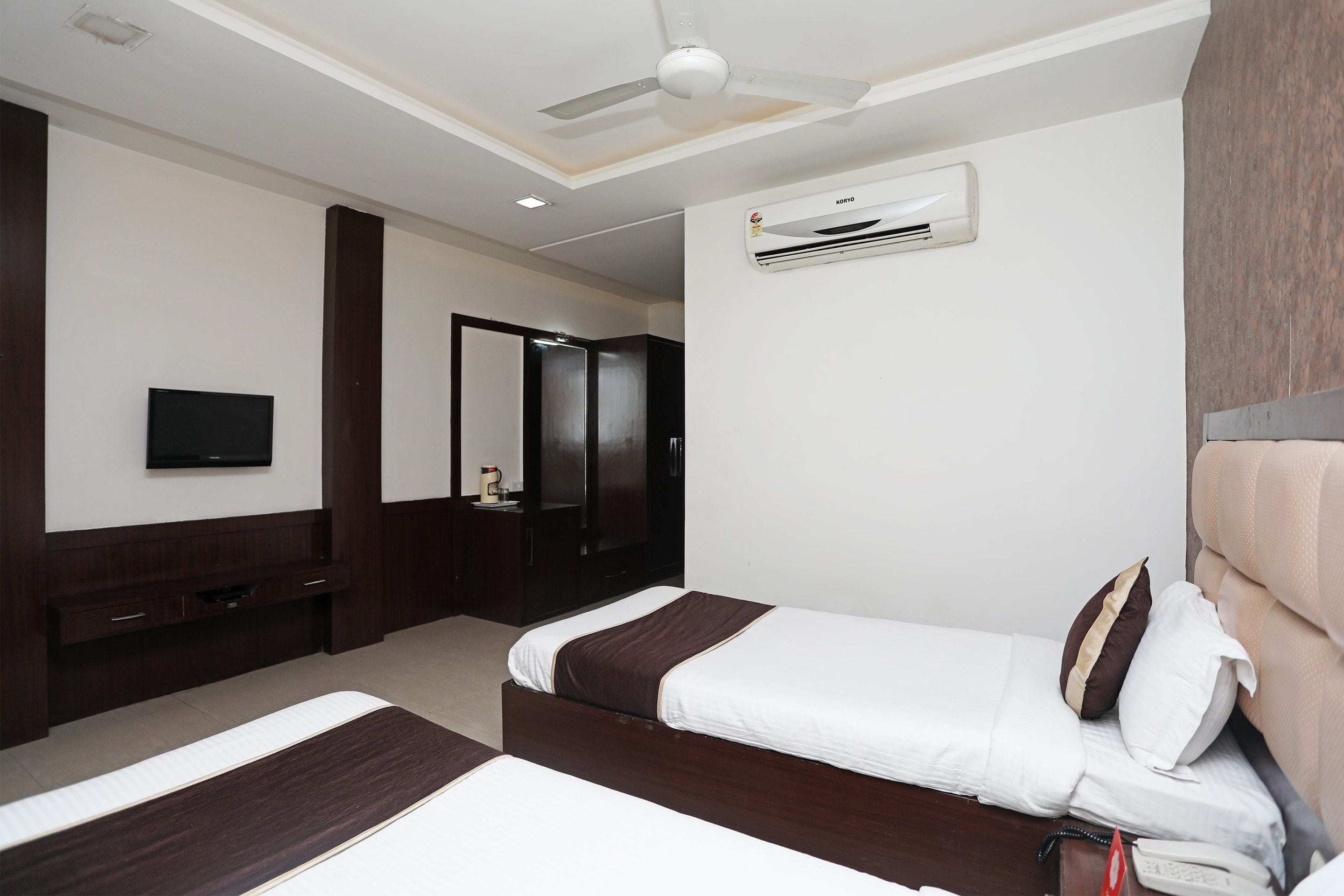 Quarto de hotel com duas camas, televisão, guarda-roupa e ar condicionado.