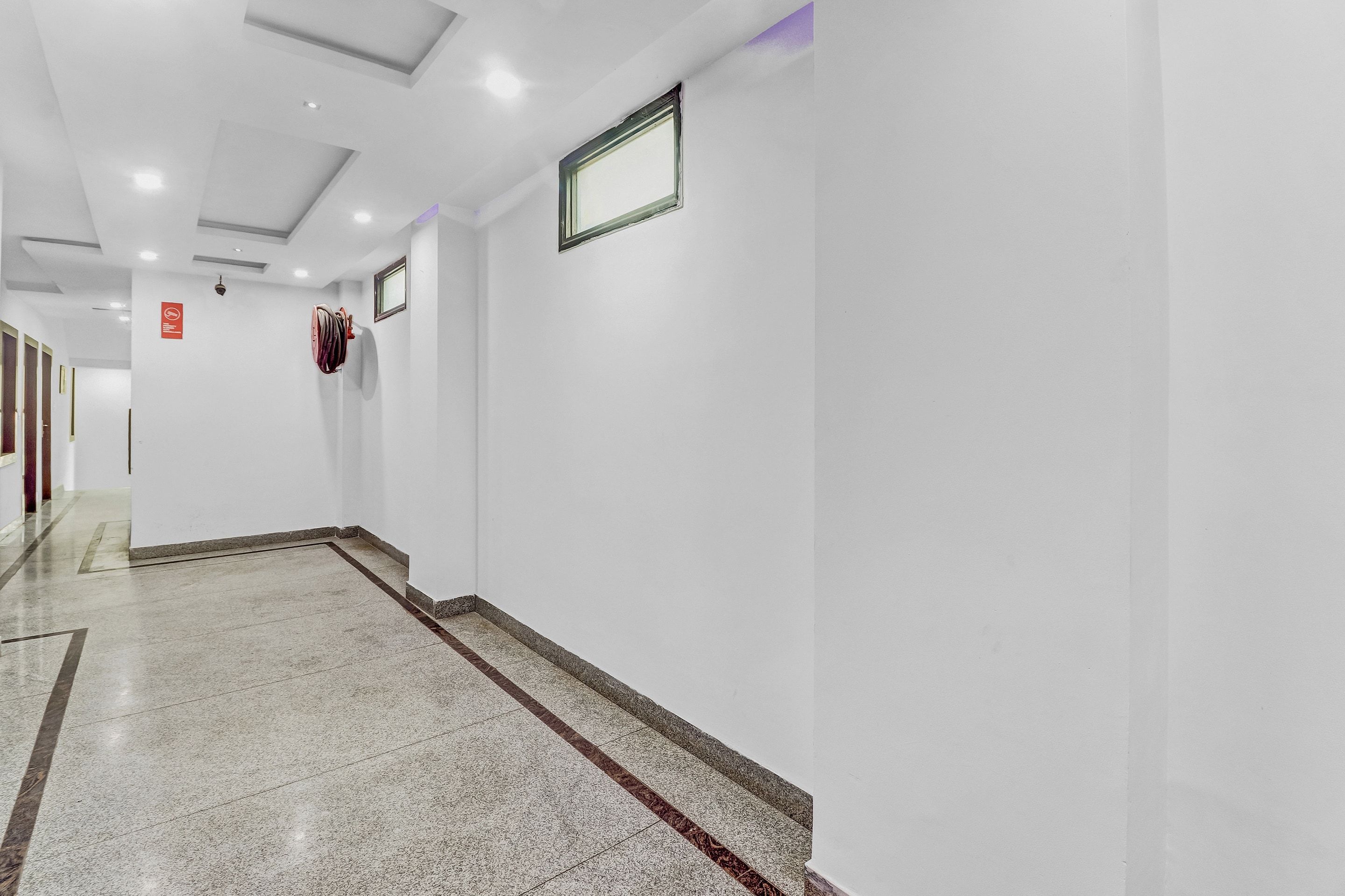 Um corredor com paredes brancas, chão ladrilhado e um hidrante fixado na parede.