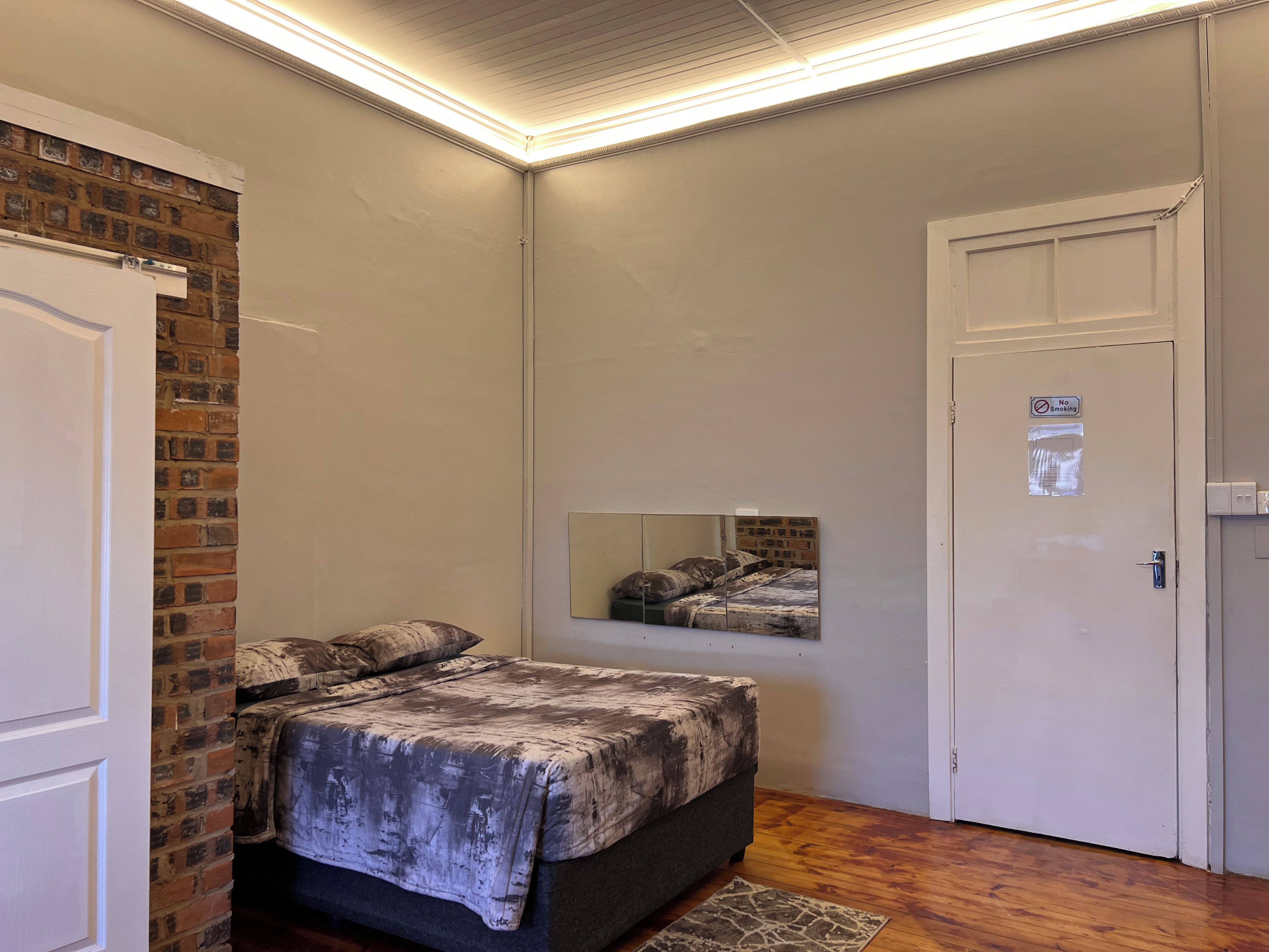 Quarto com cama, espelho, porta e parede de tijolos.