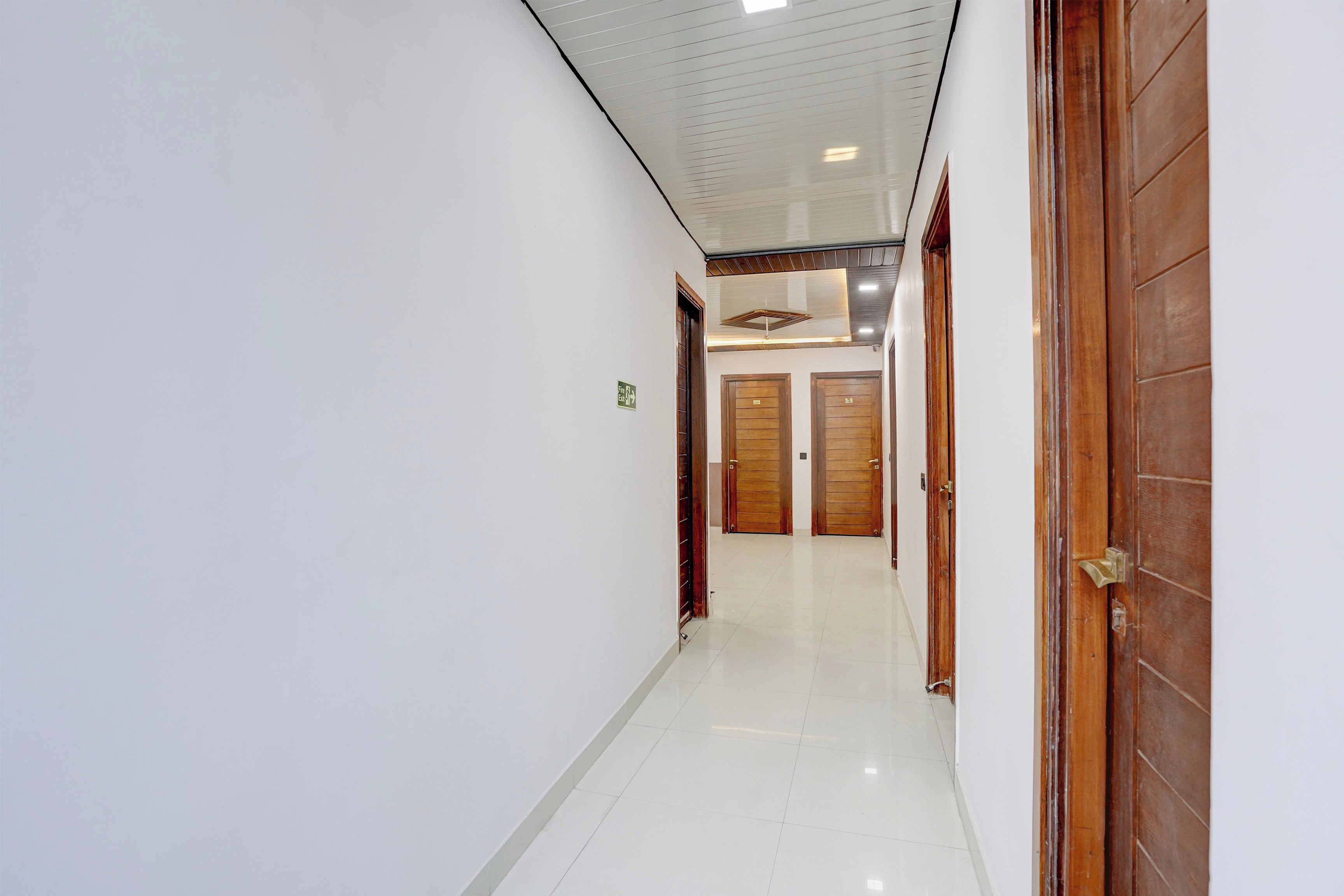 Um corredor com paredes brancas, portas de madeira e chão de azulejos.