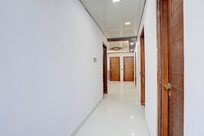 Um corredor com paredes brancas, portas de madeira e chão de azulejos.
