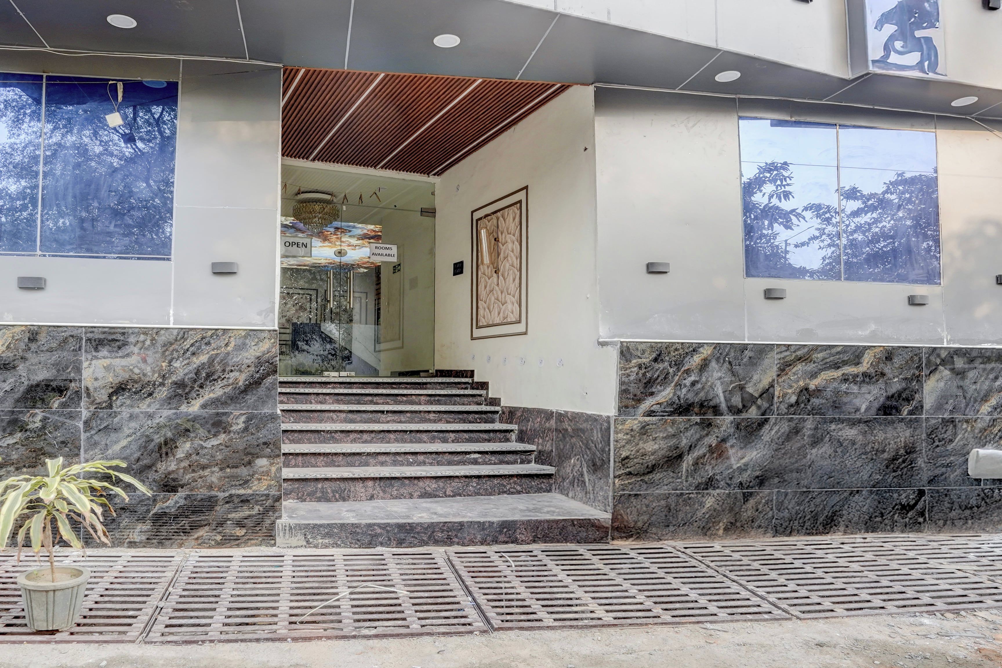 Entrada de hotel com degraus de mármore, um aviso indicando quartos disponíveis e vista para árvores pelas janelas.