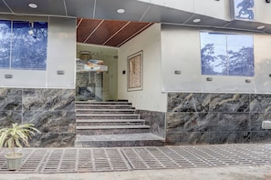 Entrada de hotel com degraus de mármore, um aviso indicando quartos disponíveis e vista para árvores pelas janelas.