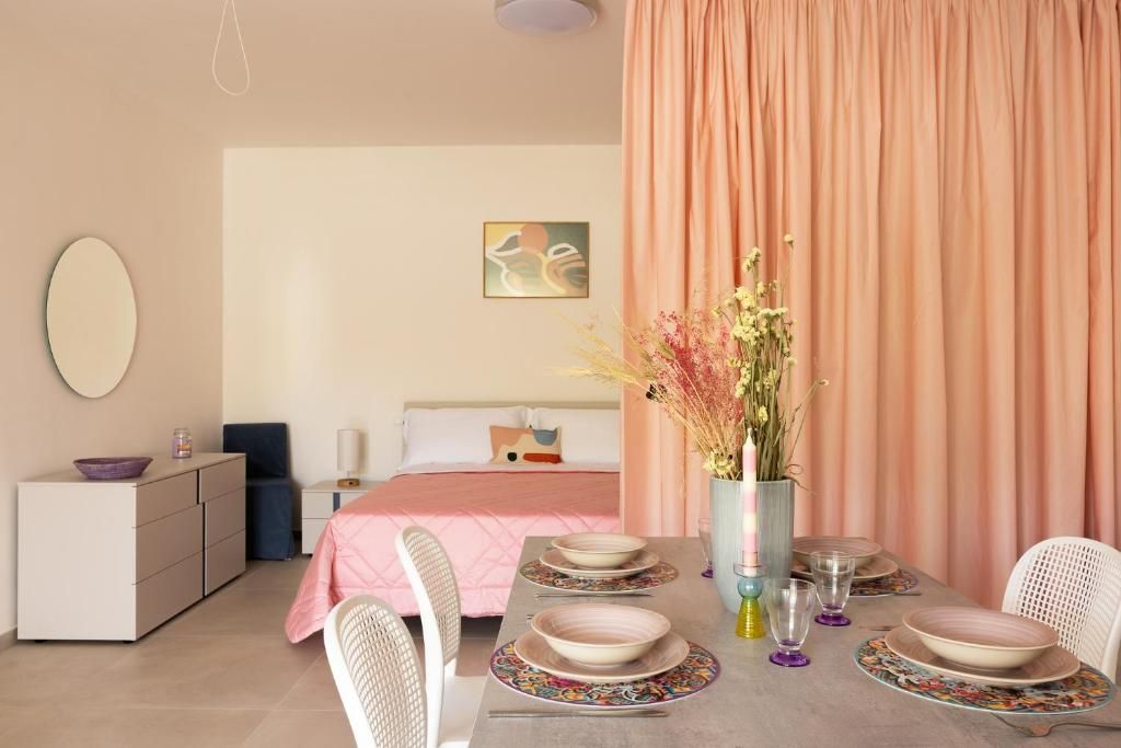 Quarto de hotel com uma cama, uma mesa de jantar posta com pratos e copos, um vaso com flores e uma obra de arte pendurada na parede.