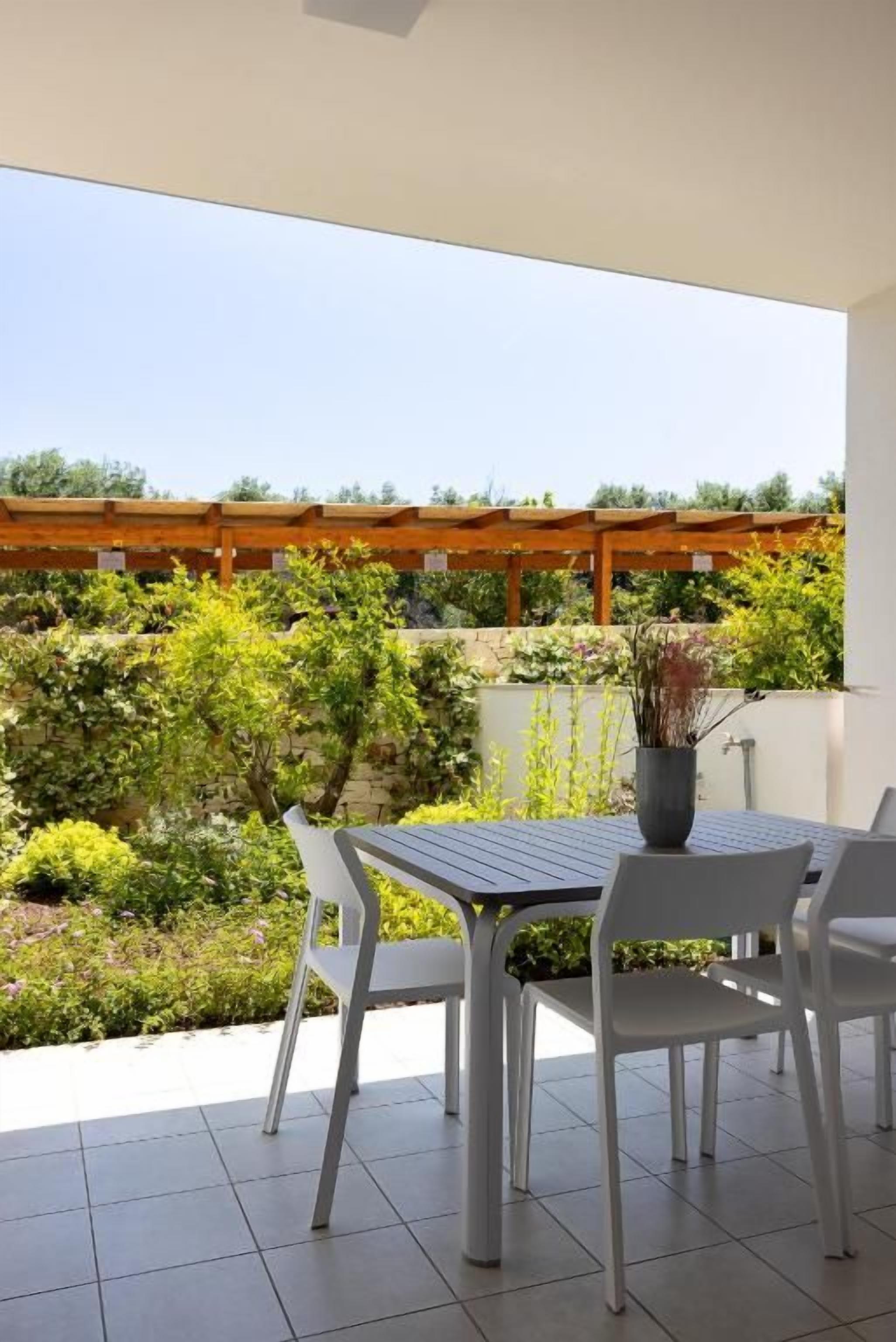 Um pátio com mesa e cadeiras, uma pérgola e vista para o jardim.