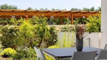 Um pátio com mesa e cadeiras, uma pérgola e vista para o jardim.