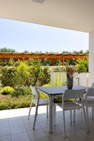 Um pátio com mesa e cadeiras, uma pérgola e vista para o jardim.