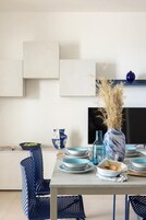 Uma área de refeições com uma mesa posta para dois, com um vaso de plantas secas, pratos azuis e cadeiras azuis combinando.