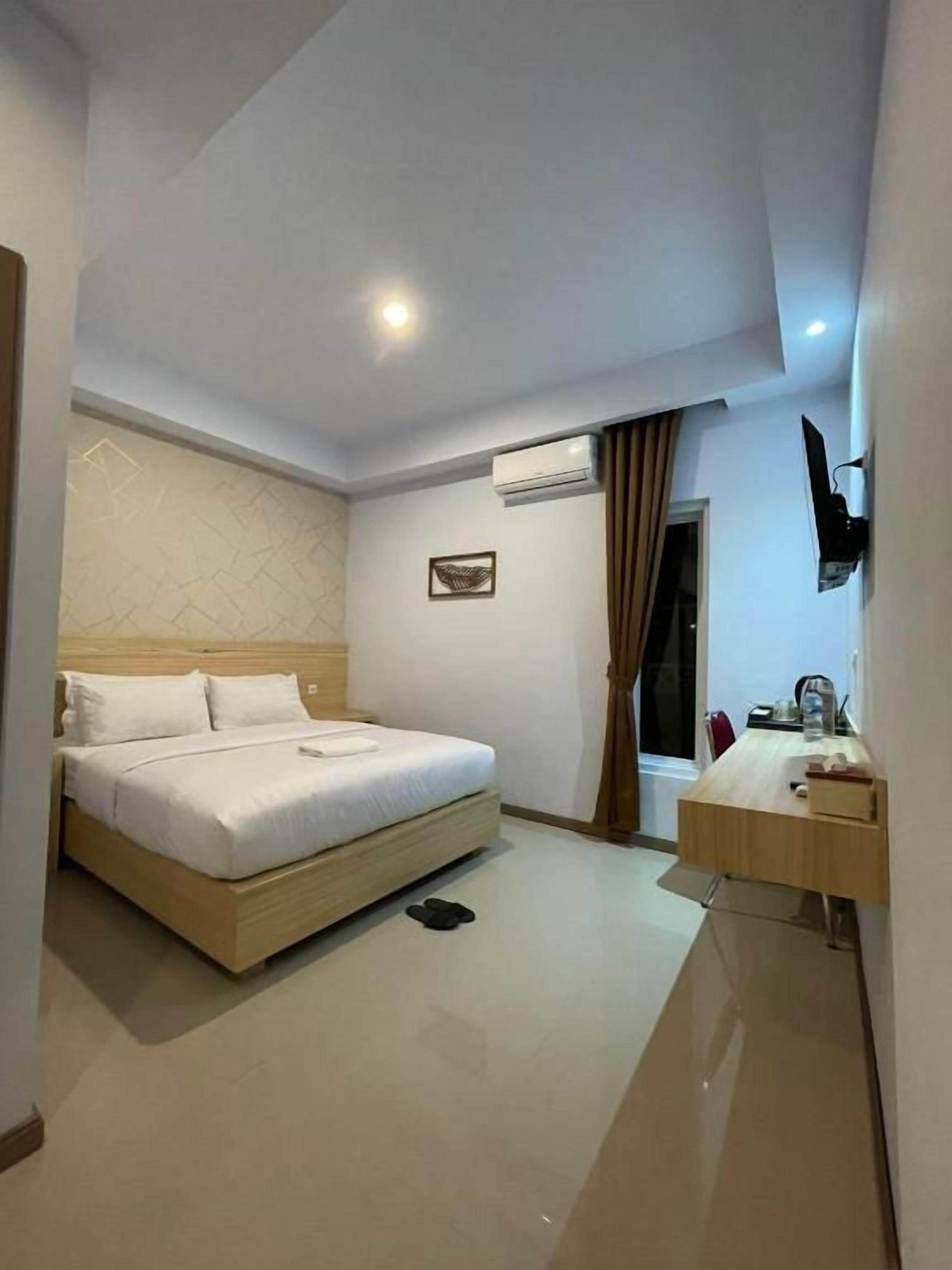 Quarto de hotel com cama, mesa de cabeceira, espelho e televisão na parede.