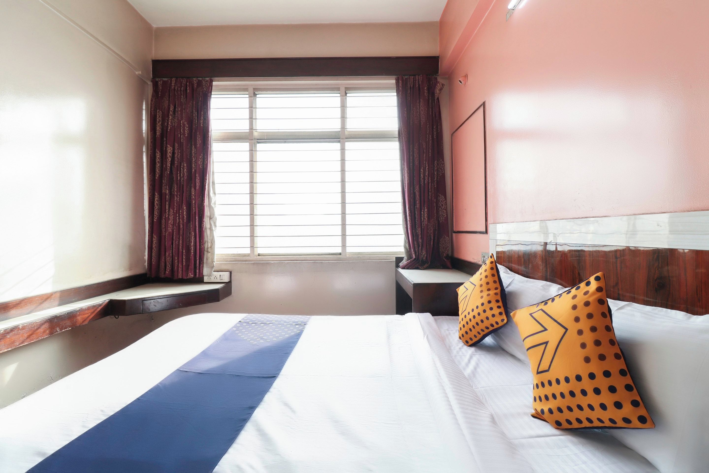 Quarto de hotel com cama, janela com cortinas, mesa de cabeceira e TV fixada na parede.