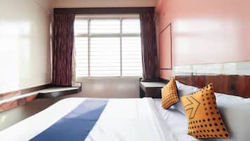 Quarto de hotel com cama, janela com cortinas, mesa de cabeceira e TV fixada na parede.