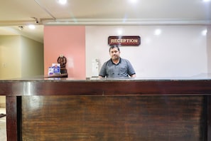 Bancada de recepção com uma placa 'RECEPTION' acima, uma estátua e alguns cartões informativos no balcão.