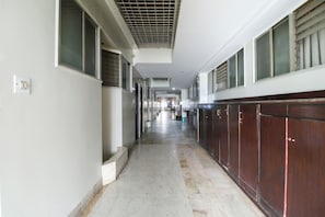 Um corredor comprido e estreito com piso de azulejos, painéis de madeira em uma lateral e uma fileira de janelas ao longo do comprimento.