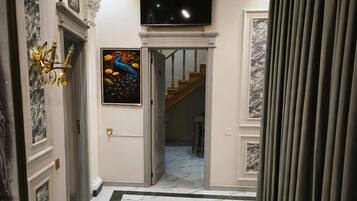 Um corredor com piso de mármore, uma TV de tela plana instalada acima de uma porta e uma escada que leva a outro cômodo.