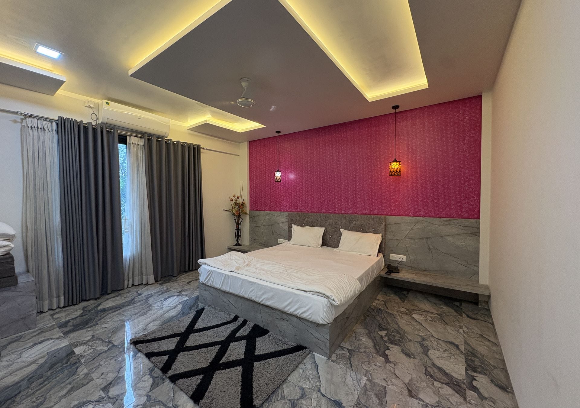 Quarto moderno com cama, piso de mármore, parede texturizada em vermelho e teto com iluminação embutida.