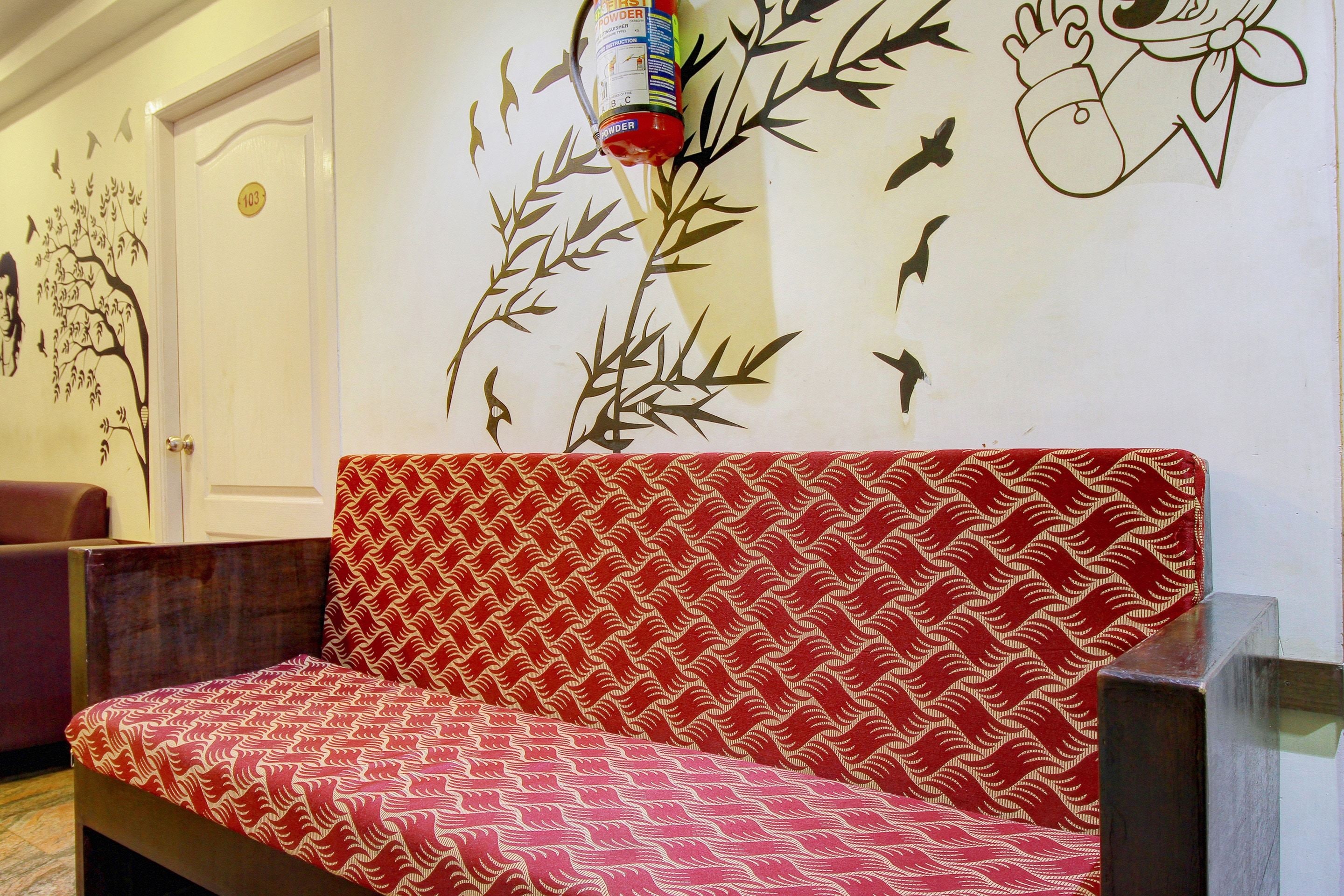 Um sofá vermelho com padrão numa sala com um mural na parede e uma porta com número.