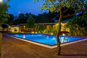 Piscina com superfície de água azul límpida, rodeada por um deck pavimentado e uma árvore.