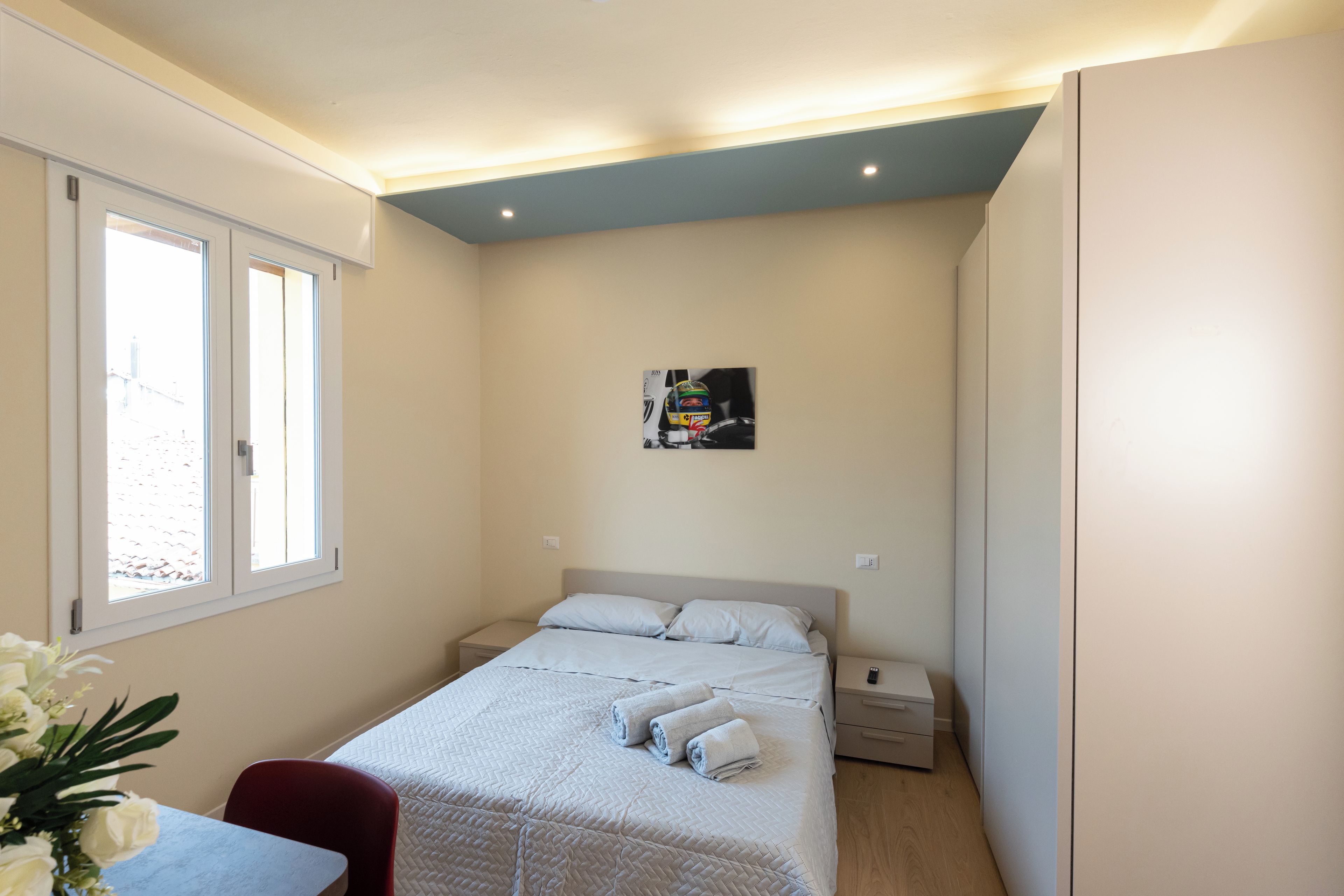 Quarto com cama, mesas de cabeceira, janela e um quadro na parede.