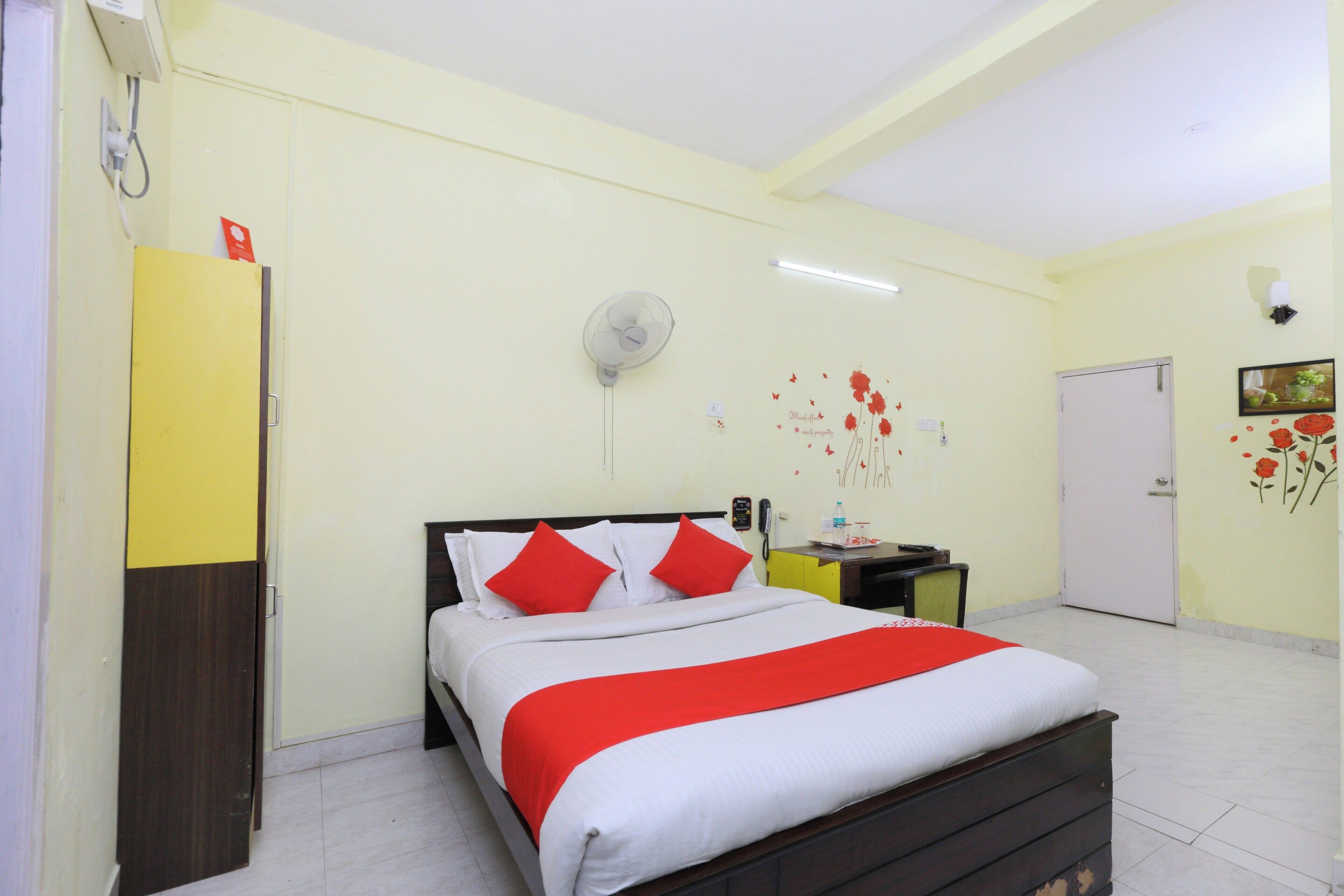 Quarto de hotel com cama, mesa de cabeceira e ventoinha fixada na parede.