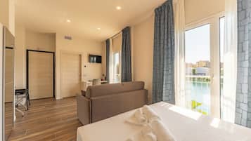 Quarto de hotel com cama, sofá, televisão, varanda com vista e porta.