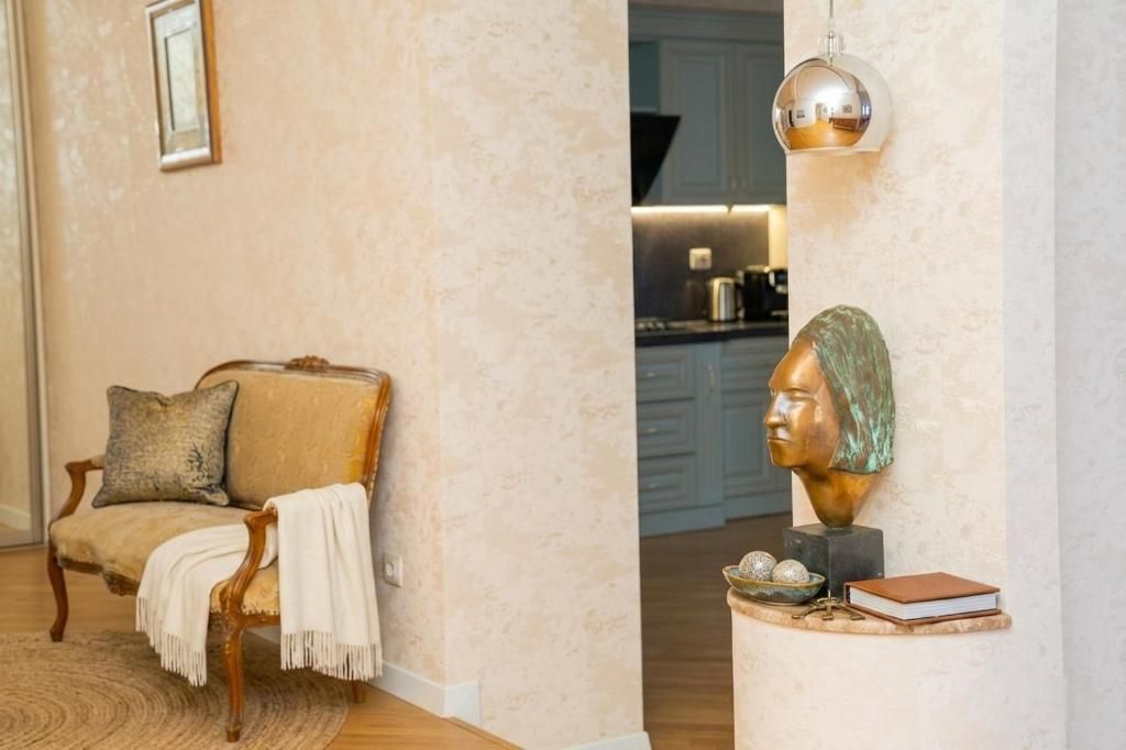 Uma sala de estar com um sofá, uma escultura de busto e uma mesinha de apoio com um livro e objetos decorativos.