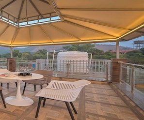 Um pátio externo com mesa, cadeiras, churrasqueira e vista para a paisagem ao redor.