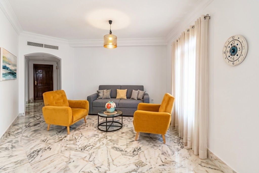 Sala de estar com sofá, duas poltronas, mesa de centro e relógio de parede.