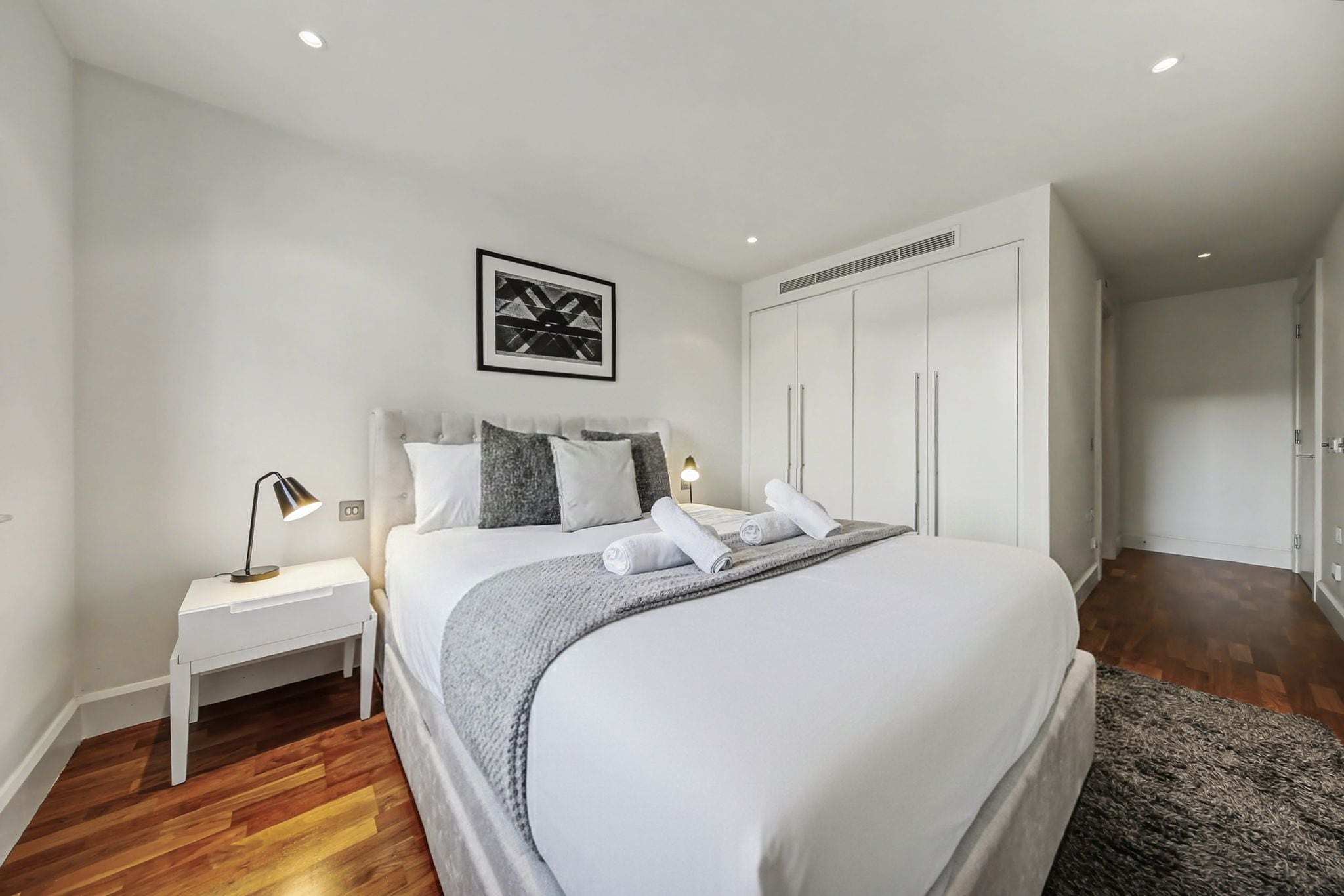 Quarto moderno com uma cama grande, mesa de cabeceira, luminária, guarda-roupa e um quadro na parede.