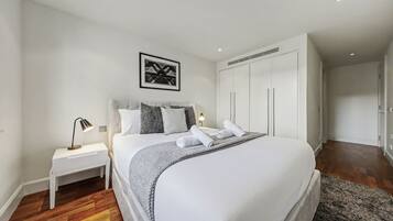 Quarto moderno com uma cama grande, mesa de cabeceira, luminária, guarda-roupa e um quadro na parede.