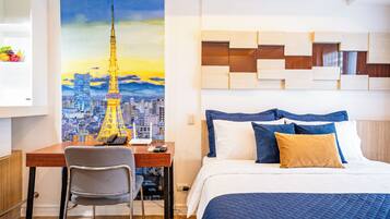 Quarto de hotel com cama, escrivaninha e cadeira. Há um quadro com vista urbana na parede.