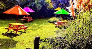 Um jardim com mesas para piquenique e guarda-sóis coloridos.