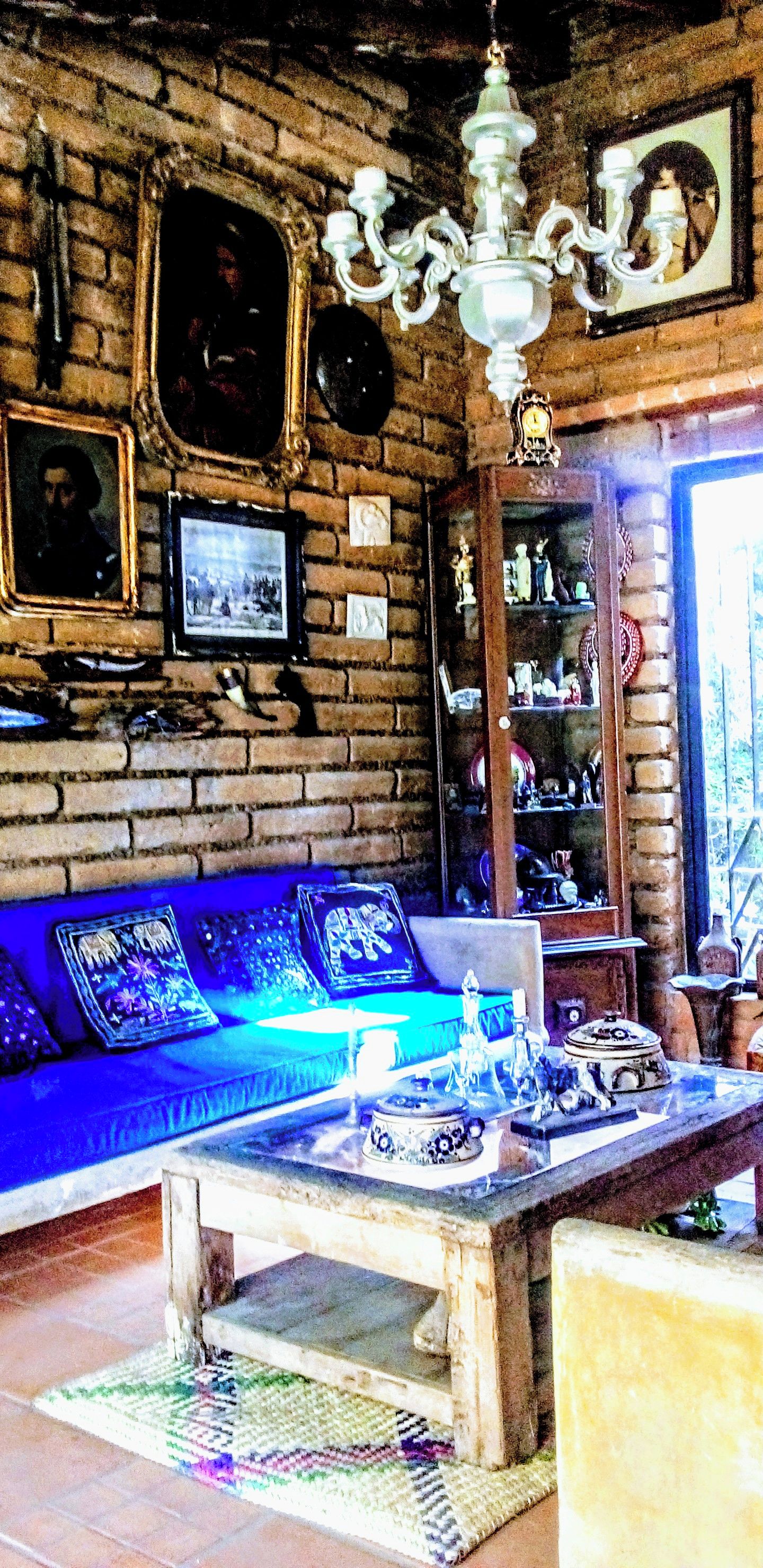 Um quarto com parede de tijolos, um sofá azul, uma mesa de centro de madeira e um candelabro.