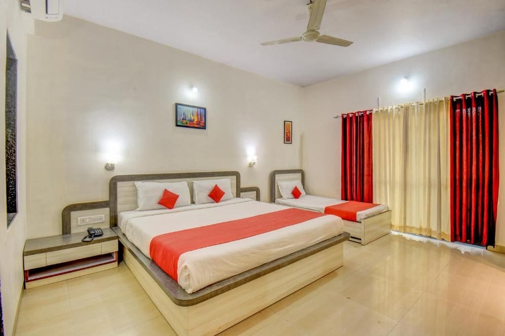 Quarto de hotel com duas camas, ventilador de teto e cortinas.