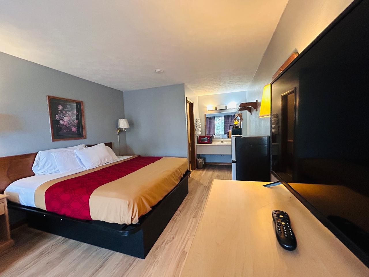 Quarto de hotel com cama, escrivaninha, televisão e espelho.