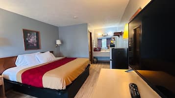 Quarto de hotel com cama, escrivaninha, televisão e espelho.